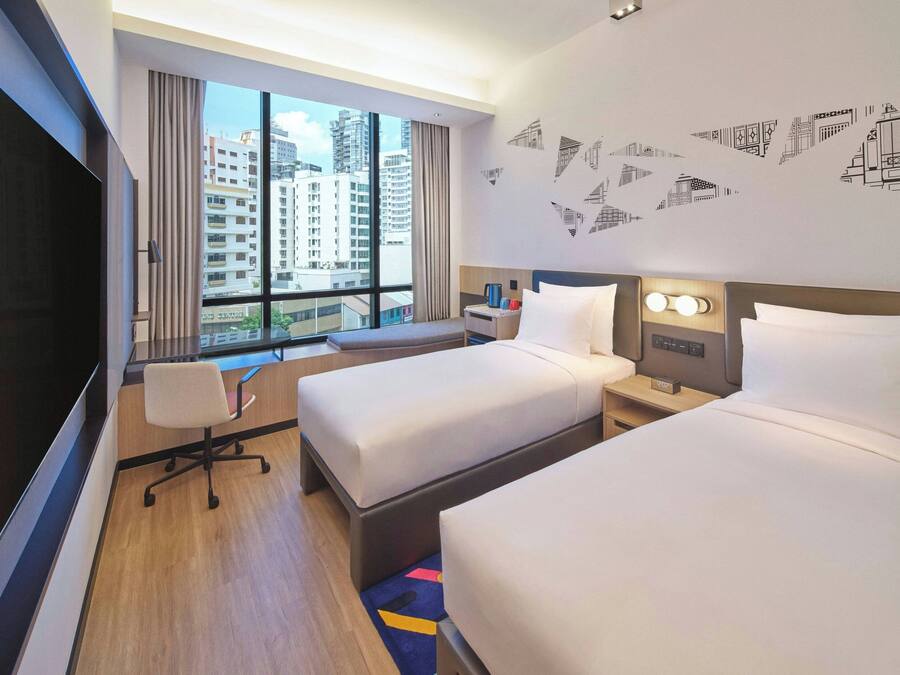 Quarto de hotel com duas camas, uma mesa, uma cadeira, uma TV e uma janela grande com vista para a cidade.