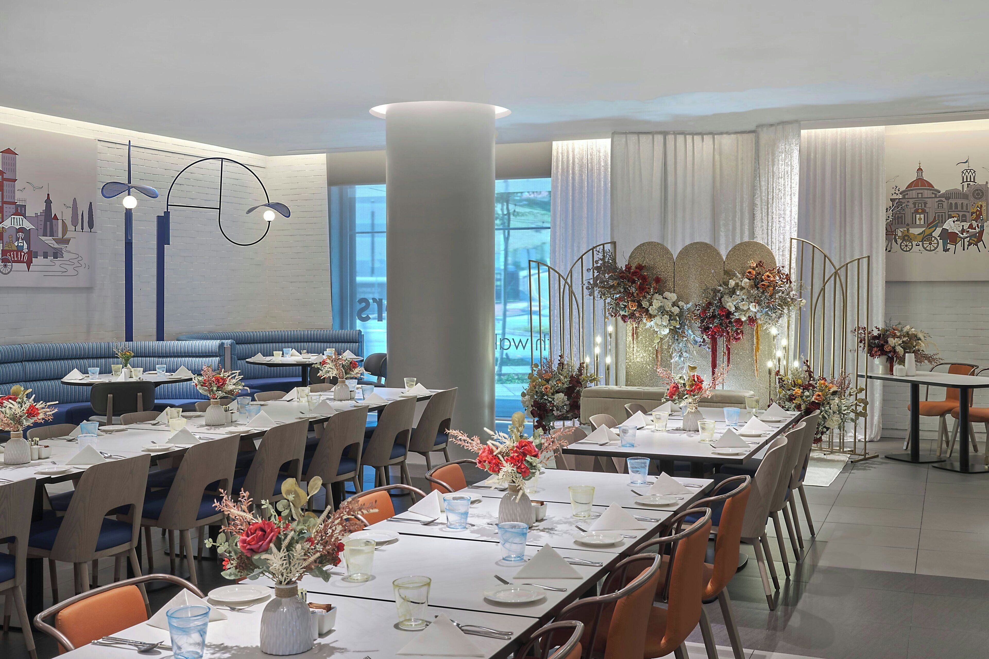 Restaurante com mesas compridas, assentos acolchoados azuis e arranjos florais decorativos.
