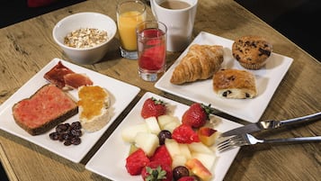 Mesa de café da manhã com torradas, geleia, frutas, croissants, muffins e uma xícara de café.