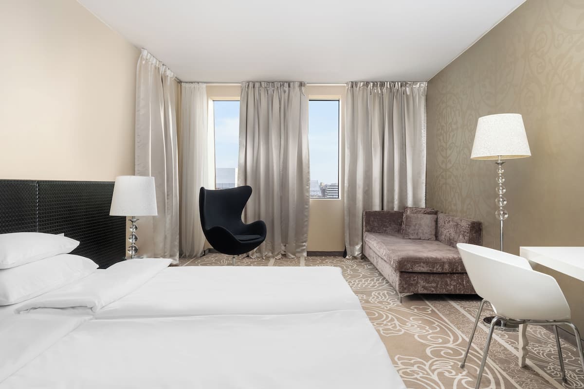 Quarto de hotel com uma cama, uma cadeira, um sofá, uma mesa e uma luminária.