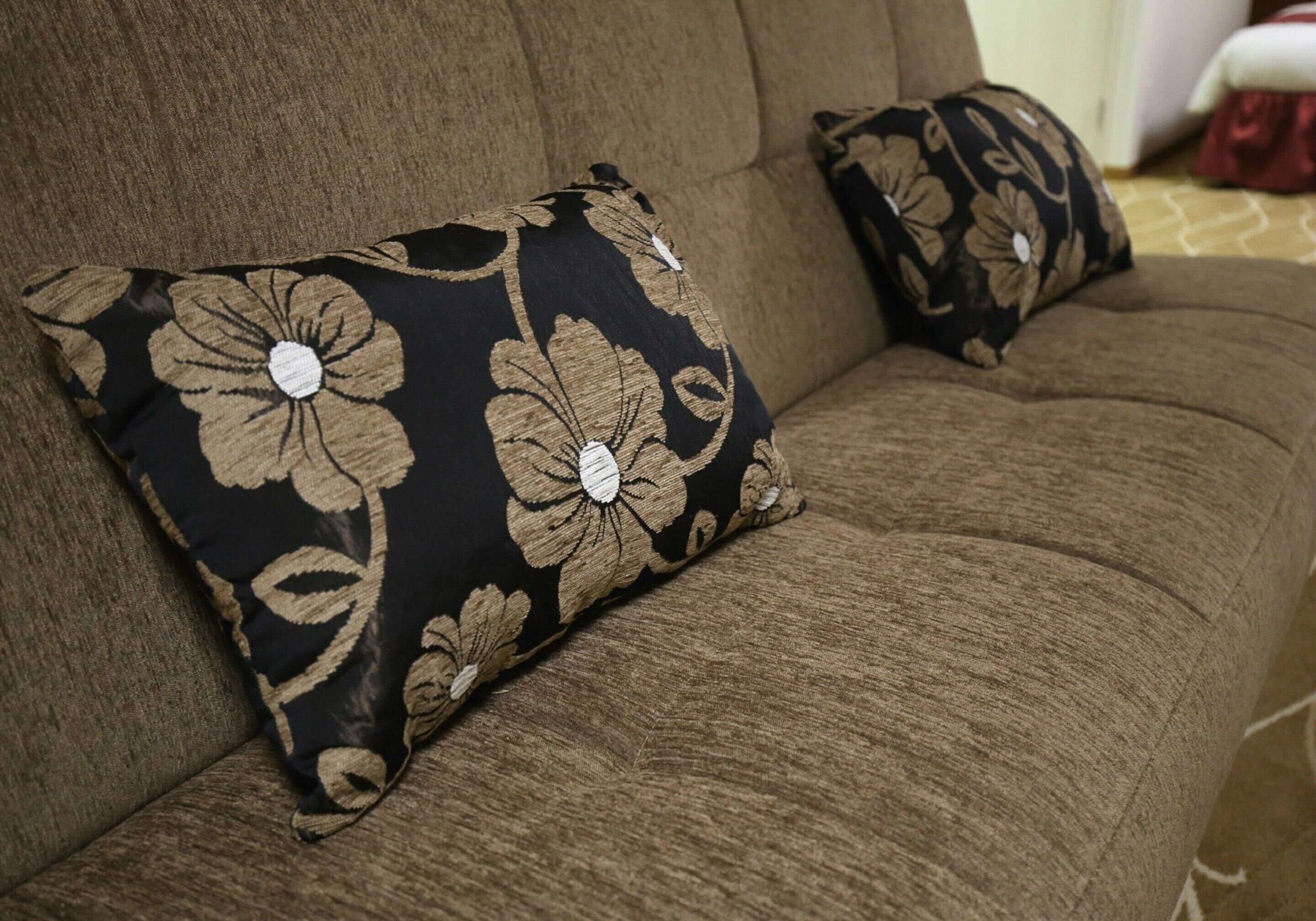 Um sofá marrom com duas almofadas decorativas com padrão floral preto e bege.