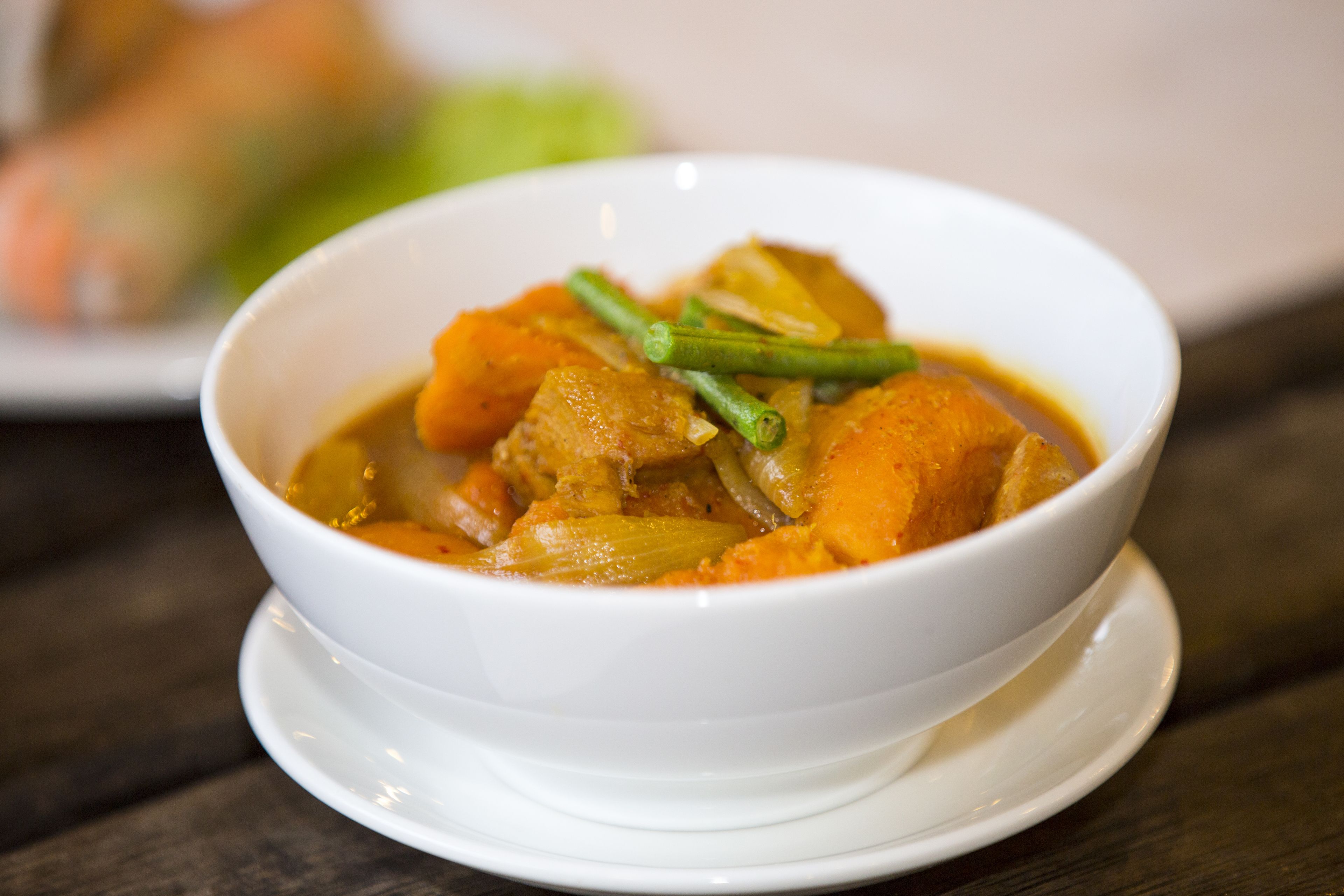Uma tigela branca de curry com legumes e cebolinha sobre um pires branco.