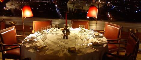 Mesa de jantar redonda posta para uma refeição, com vista para a cidade ao fundo.