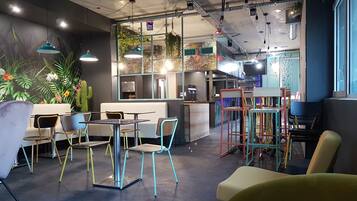 Um café moderno com diversas opções de assento, incluindo mesas e cadeiras, e uma grande janela com vista para o verde.