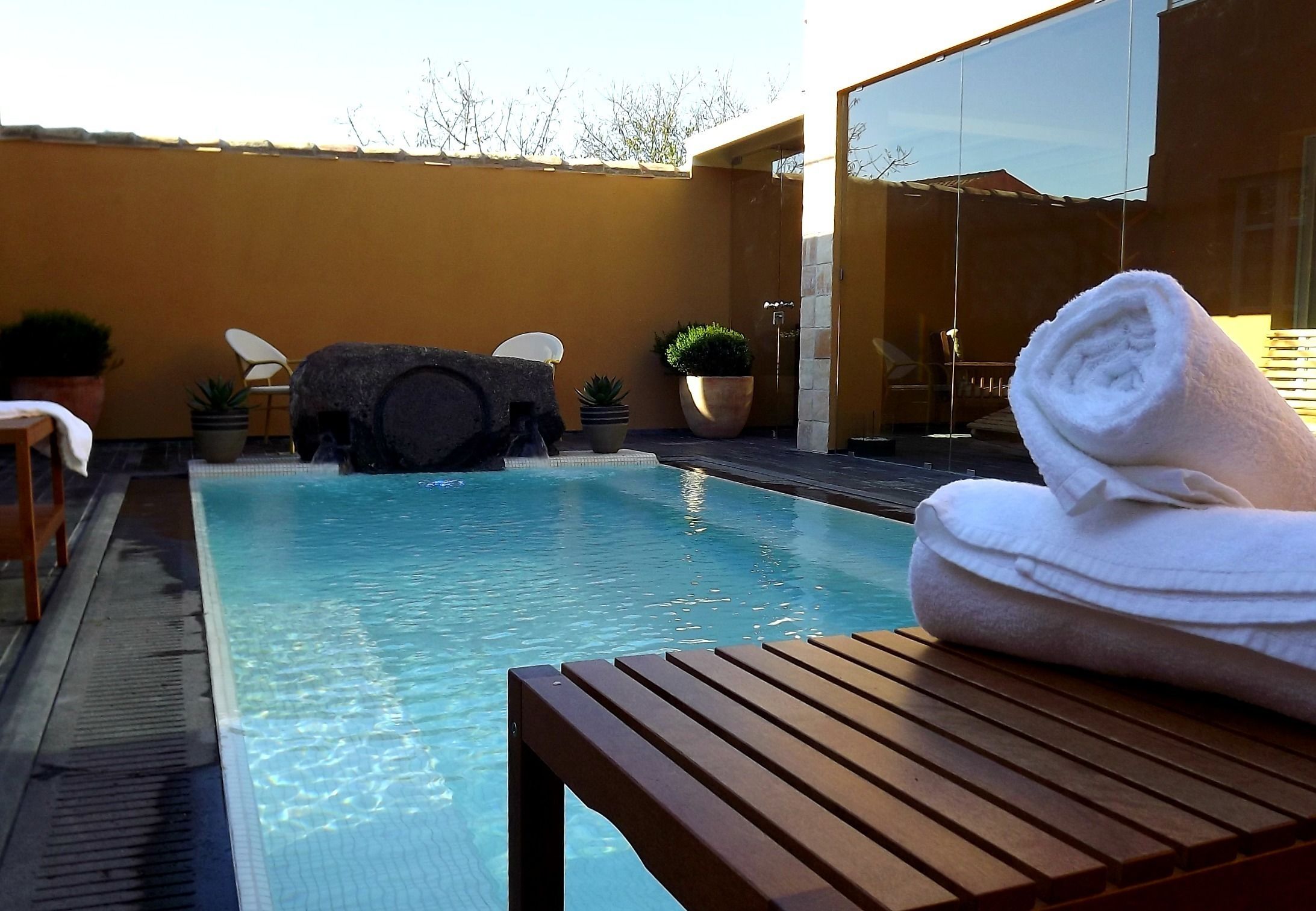 Uma piscina com deck de madeira, um elemento decorativo em pedra e uma toalha sobre um banco.
