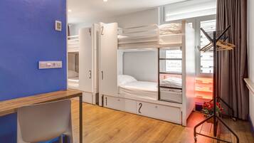 Quarto de hotel com beliches, uma escrivaninha e uma cadeira.