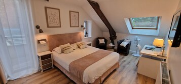Quarto com uma cama grande, uma escrivaninha com abajur, uma cadeira e uma janela.