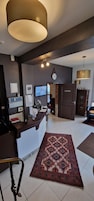 Uma área de recepção com balcão, relógio, televisão e mesa de atendimento.
