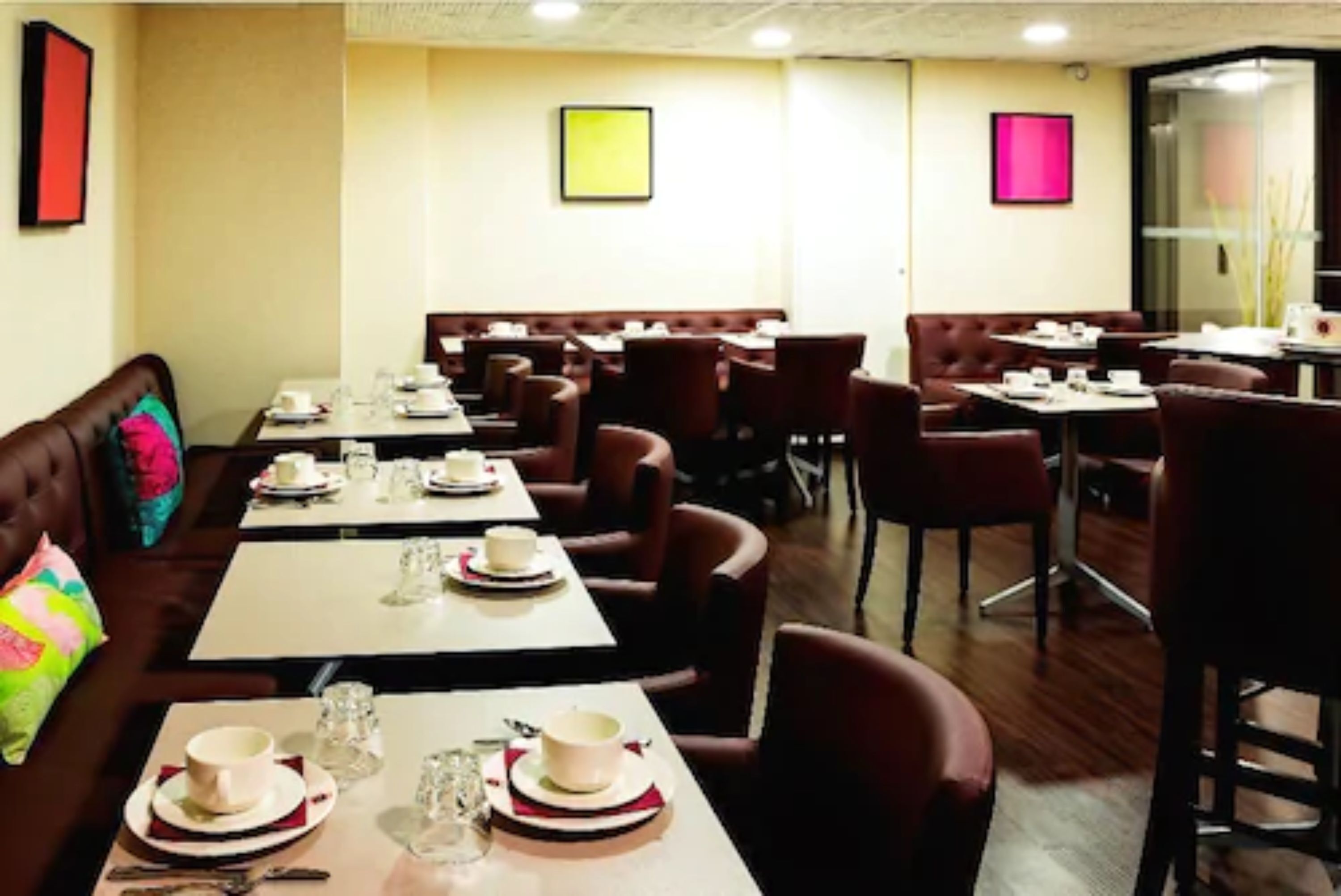 Um restaurante com cabines e mesas, cada conjunto com pratos, copos e talheres.