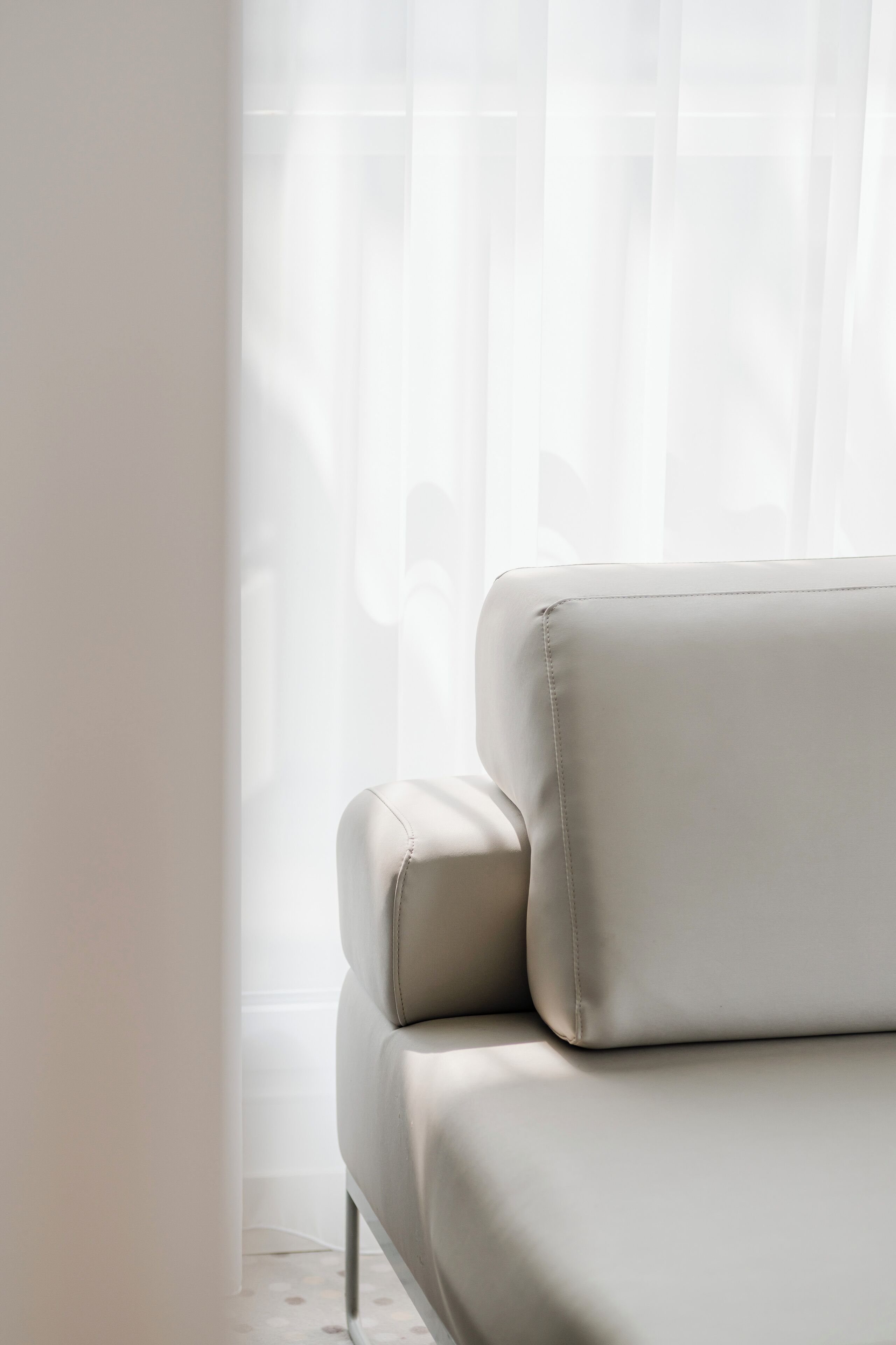 Uma sala de estar moderna e minimalista, com um sofá de cor clara e cortinas leves.