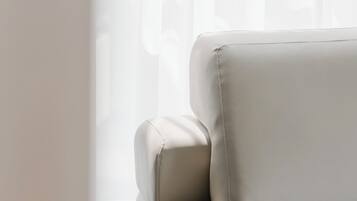 Uma sala de estar moderna e minimalista, com um sofá de cor clara e cortinas leves.