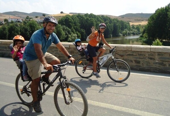 Um grupo de pessoas andando de bicicleta sobre uma ponte, com um rio e colinas ao fundo.