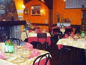 Restaurante com várias mesas preparadas para refeições, destacando um interior acolhedor com paredes alaranjadas e vigas de madeira.