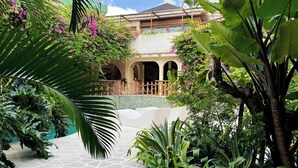 Um jardim tropical com um caminho de pedra que leva a um edifício com arcos e uma piscina.