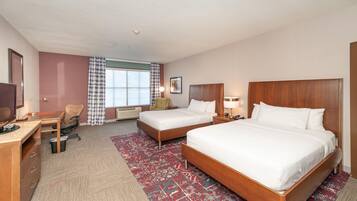Quarto de hotel com duas camas, uma escrivaninha, uma cadeira, televisão e janela com cortinas.