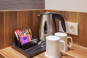 Uma área de cozinha com chaleira, canecas de café e um tabuleiro com cápsulas de café.