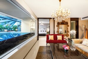 Quarto de hotel moderno com uma grande janela com vista para uma piscina, um sofá vermelho, um candelabro e um espelho com moldura ornamentada.