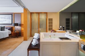 Quarto de hotel moderno com cama, mesa de cabeceira, abajur e banheiro com banheira, pia e porta-toalhas.