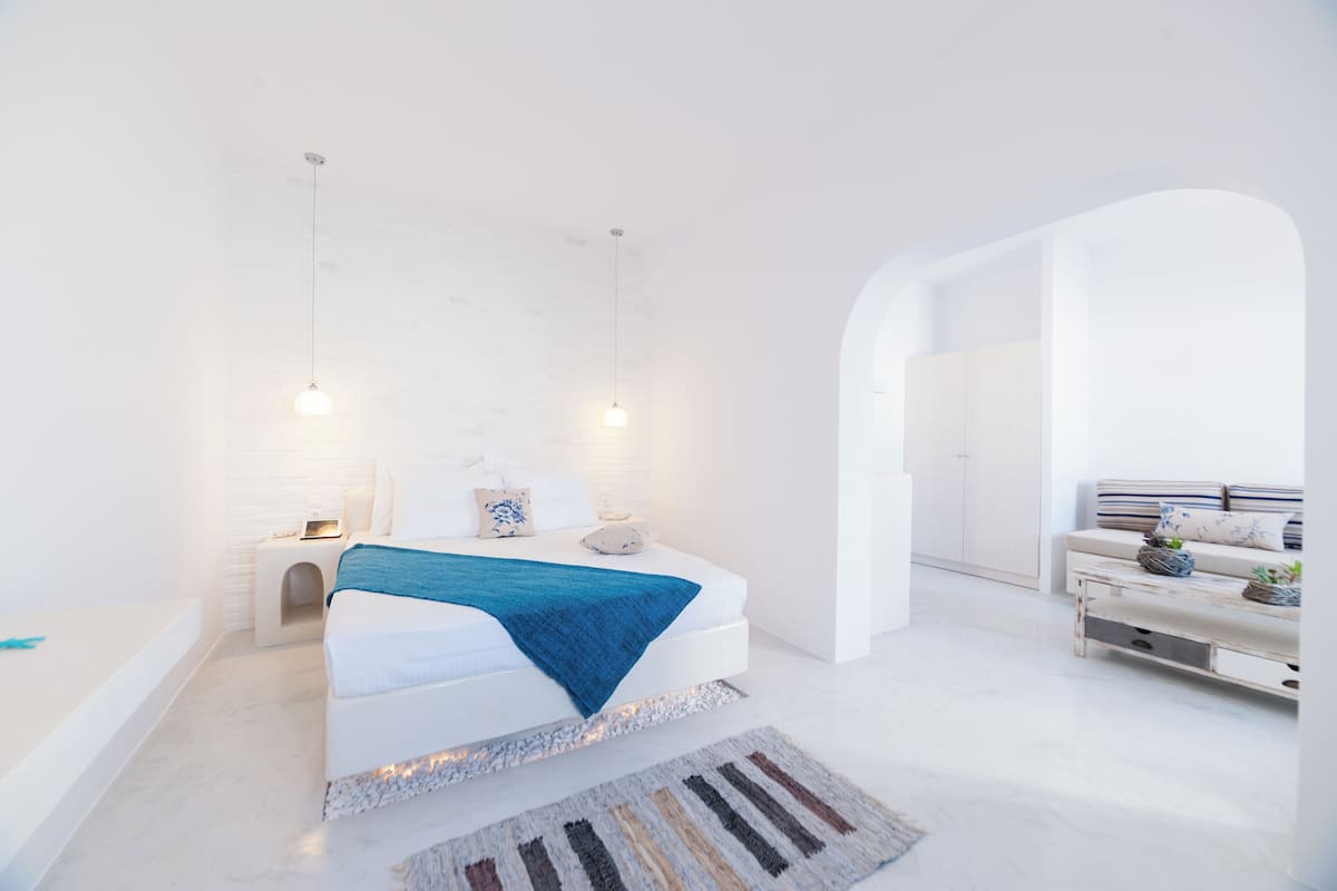 Quarto moderno e minimalista com cama branca, mesas de cabeceira e uma janela grande.