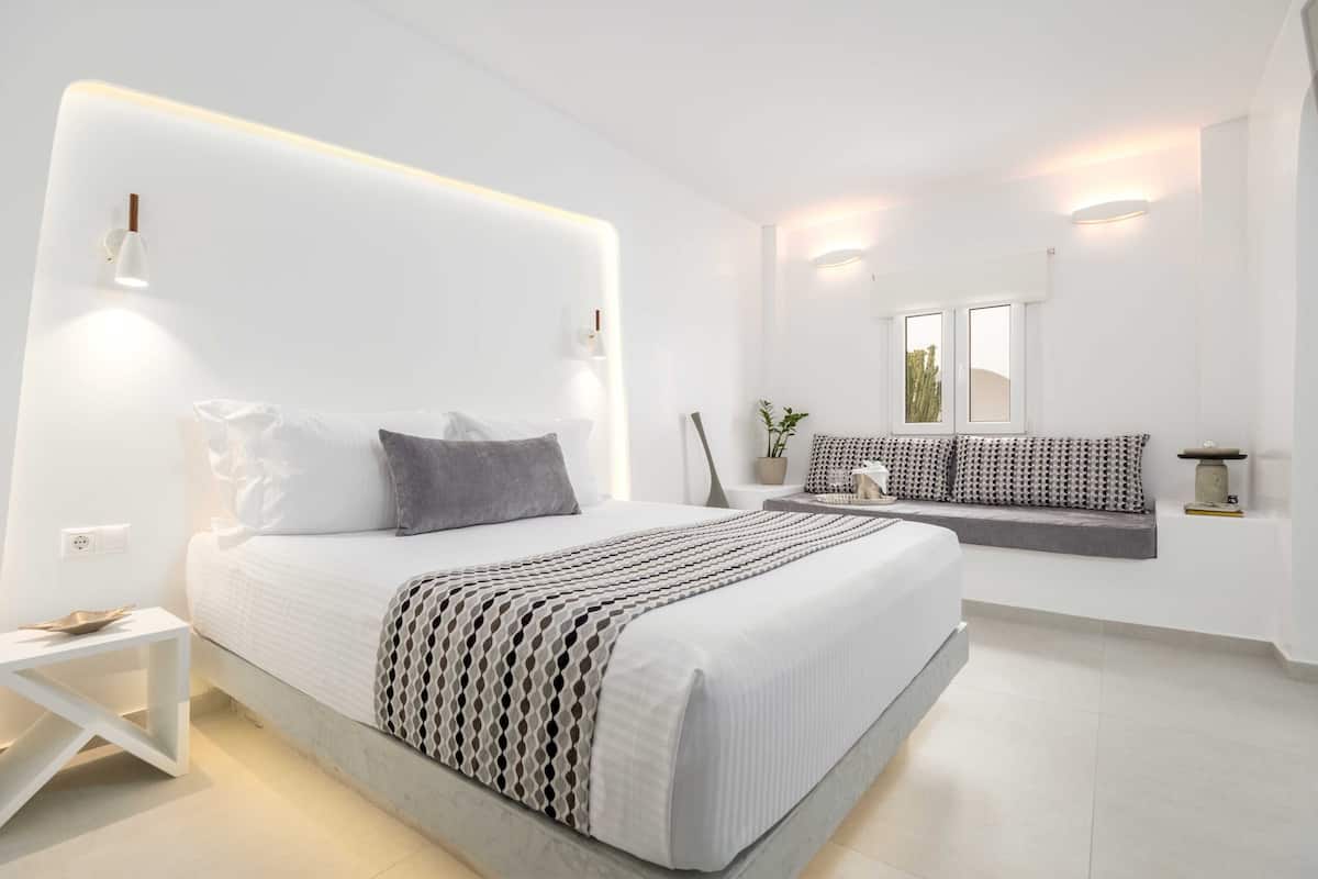 Quarto moderno com uma cama grande, mesas de cabeceira, um banco embutido e um espelho sobre o banco.