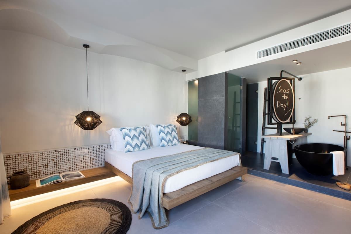 Quarto moderno com cama grande, mesas de cabeceira, banheira integrada e espelho.
