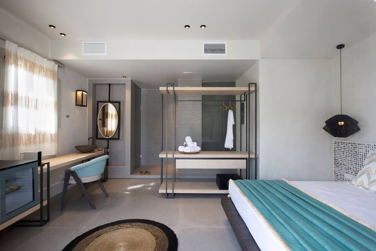 Quarto moderno com cama, escrivaninha, espelho e área de chuveiro.