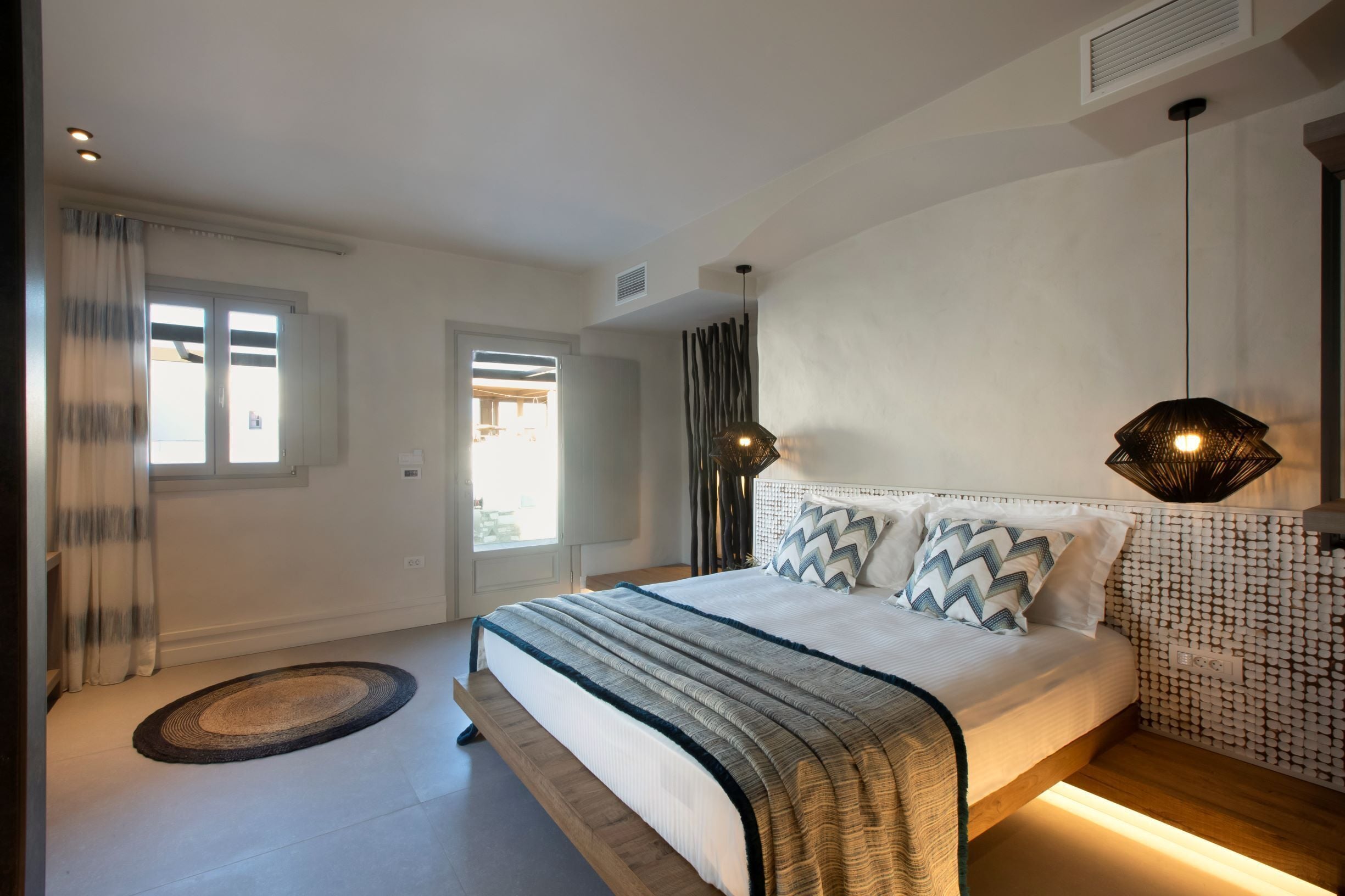 Quarto com cama, luminária de cabeceira, janela e porta.