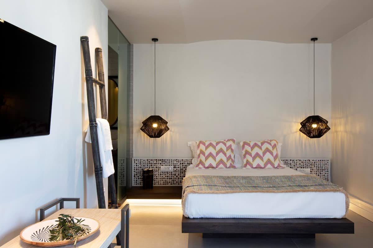 Quarto moderno com cama, luminárias de cabeceira, televisão e uma pequena mesa com uma planta.