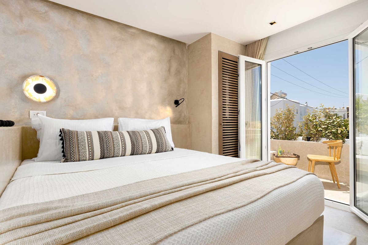 Quarto moderno com cama grande, luminária fixada na parede e vista para a varanda externa.