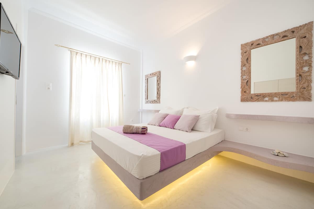 Quarto moderno com cama, mesa de cabeceira, espelho e janela com cortinas.