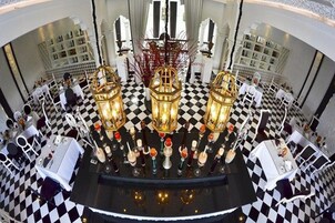 Um hall com piso xadrez, uma área decorativa central com três estruturas iluminadas e mobiliário branco.