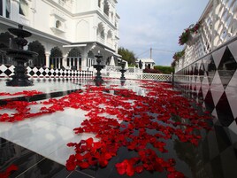 Um pátio com uma fonte, edifício branco com arcos e pétalas vermelhas no chão.