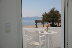 Uma varanda com uma cadeira e mesa brancas, com vista para uma praia e uma montanha ao longe.