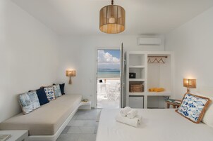 Quarto de hotel com cama, área de estar com almofadas, guarda-roupa e vista para a praia.