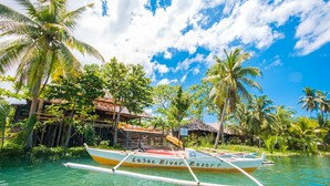 Um barco chamado 'Lobos River Resort' atracado em um resort tropical com palmeiras e edifícios com telhados de palha.