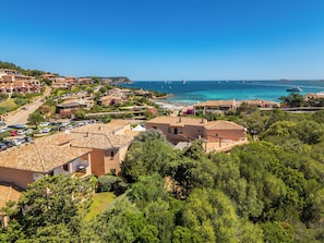 Uma cidade costeira com edifícios de telhados em terracota, um porto com barcos e um céu azul claro.