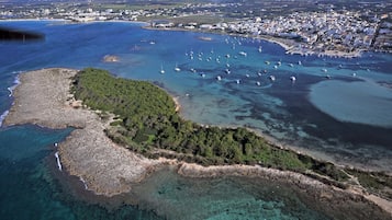 Vista aérea de uma vila costeira com um porto de iates, litoral rochoso e vegetação densa.