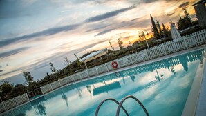 Piscina cercada por árvores e um pôr do sol, com cerca branca e boia salva-vidas.