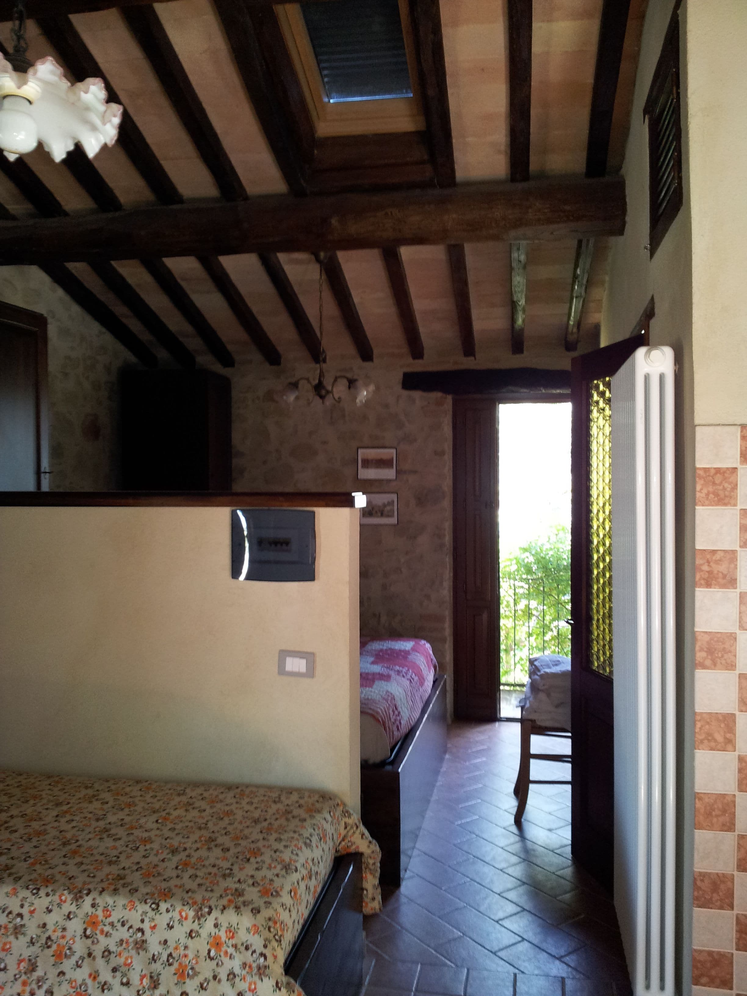 Quarto com cama, pequena escrivaninha, radiador e janela com vista para o verde.