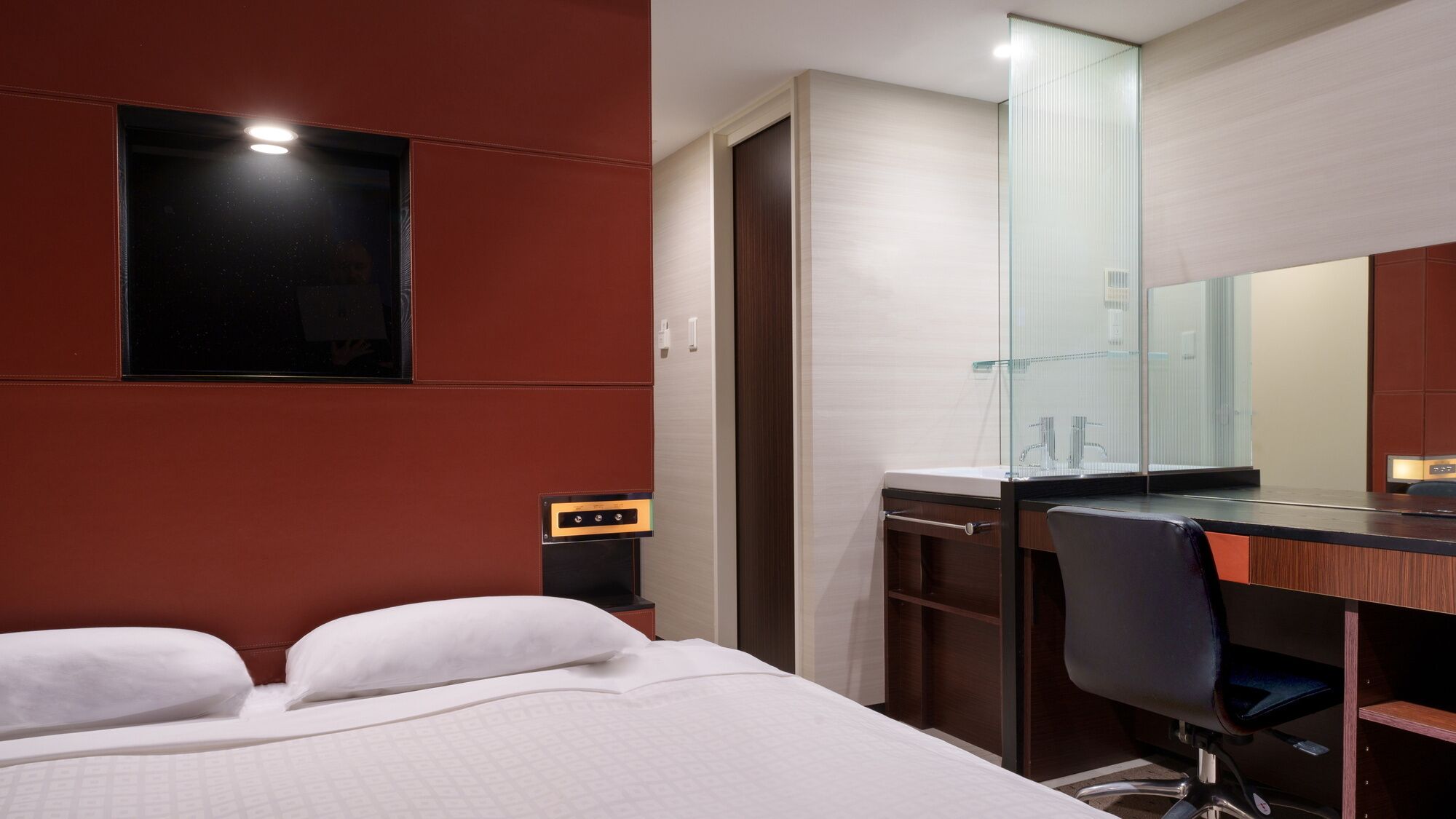 Quarto de hotel com cama, escrivaninha, espelho e guarda-roupa.