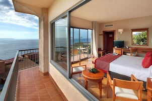 Quarto de hotel com varanda, cama, escrivaninha e televisão.