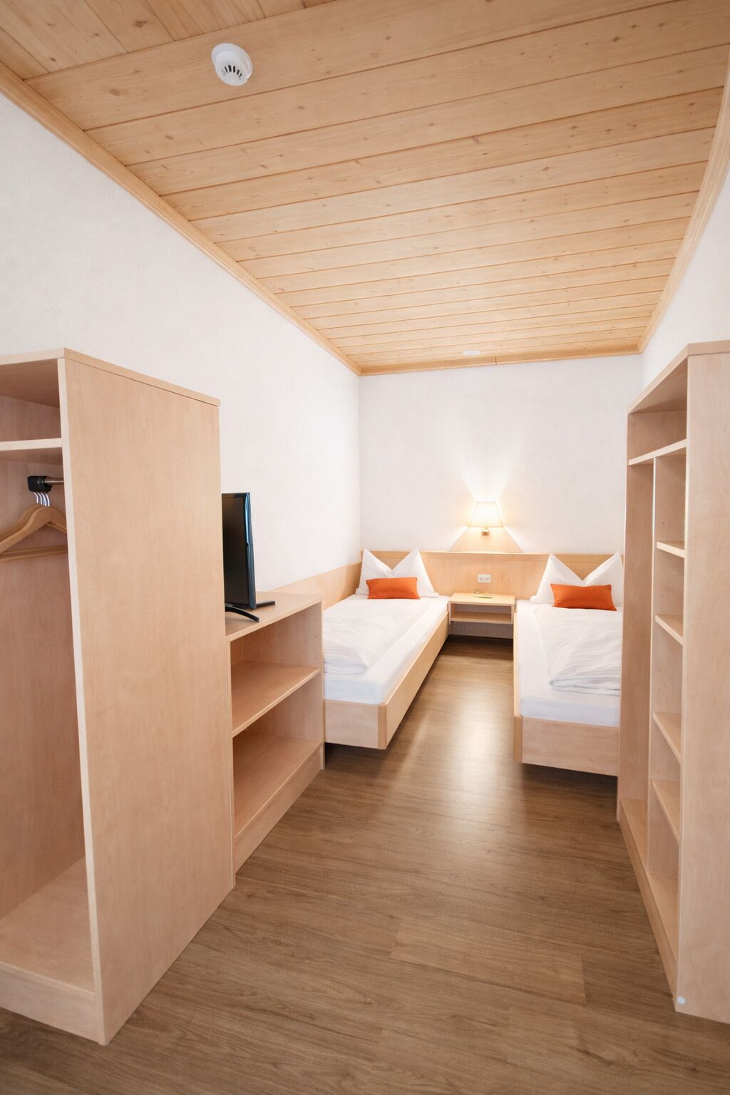 Quarto compacto com duas camas, uma escrivaninha e um guarda-roupa.