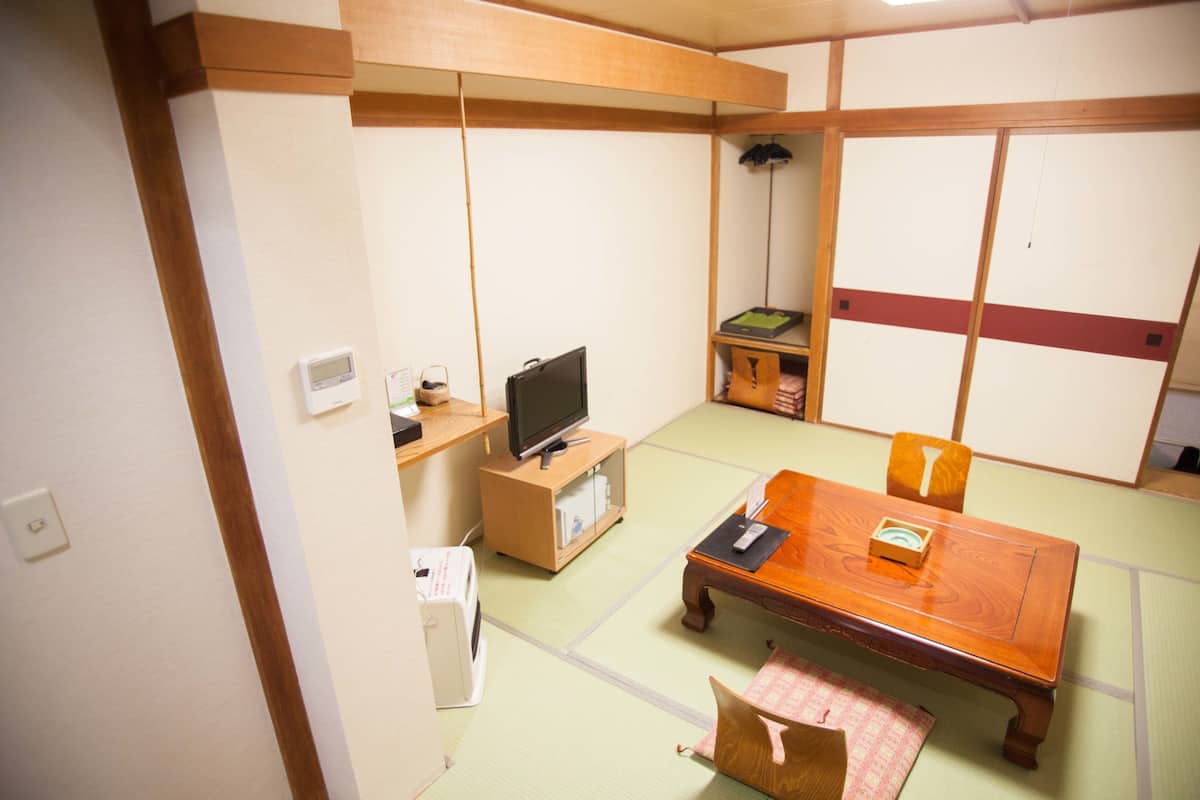 Um quarto japonês tradicional com tatames, uma mesa de madeira, uma televisão sobre um suporte baixo e uma cama futon.