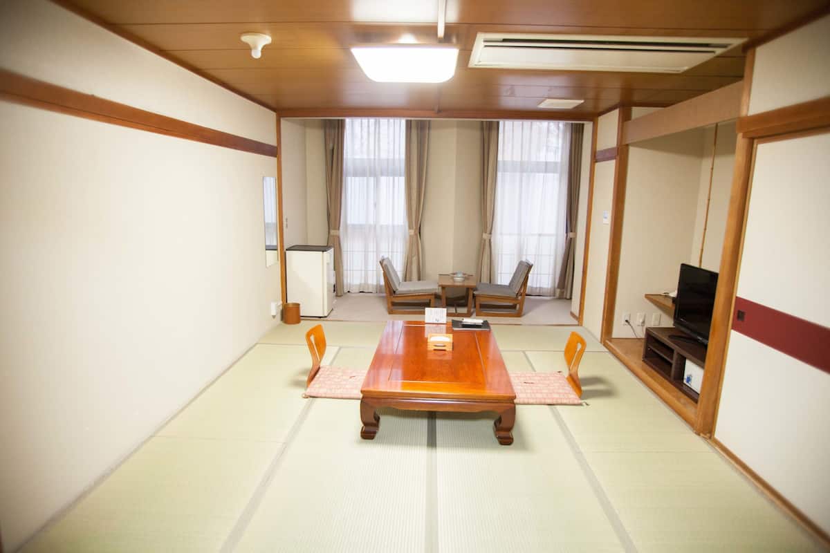 Um quarto em estilo japonês tradicional, com piso de tatame, uma mesa de madeira e uma televisão.