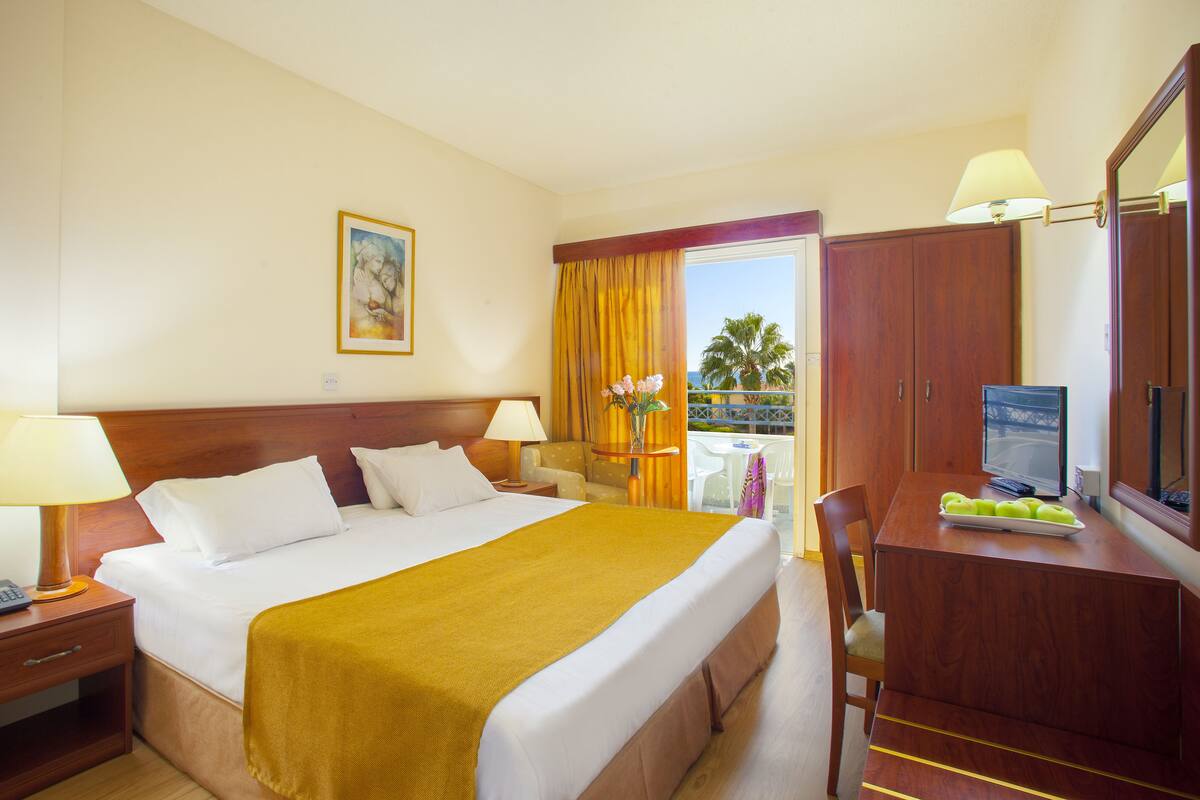 Quarto de hotel com uma cama grande, uma escrivaninha com computador, uma cadeira e vista para o exterior.