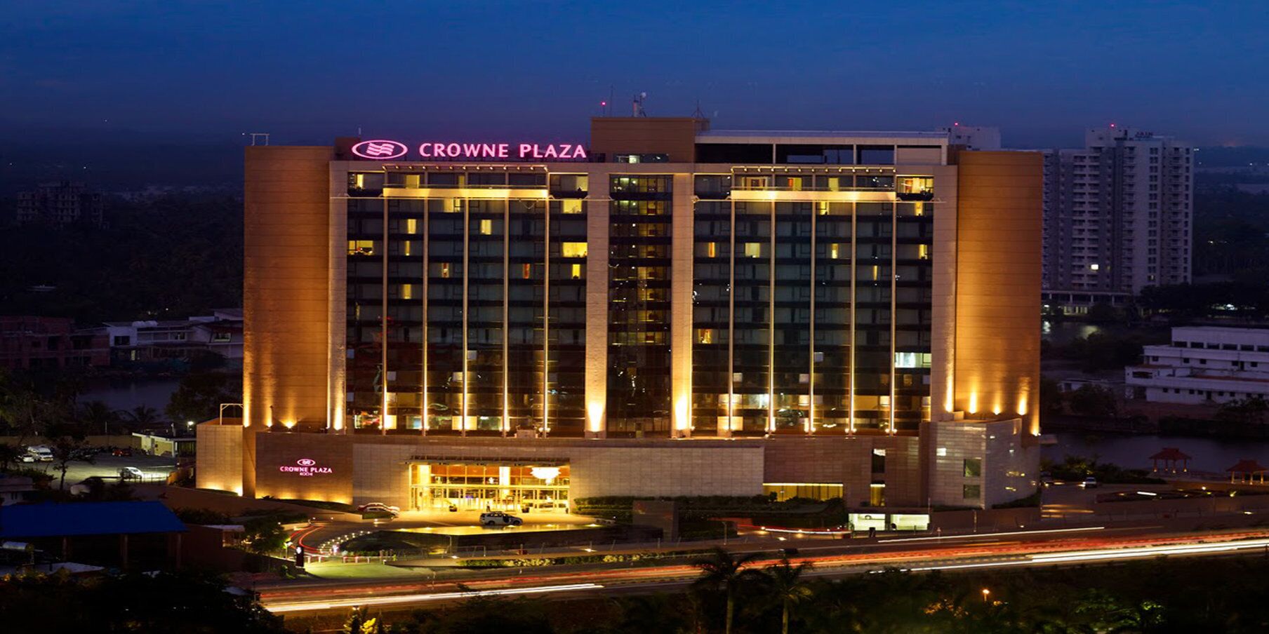 Um hotel com vários andares, um letreiro chamativo 'CROWNE PLAZA', janelas grandes e fachada bem iluminada.