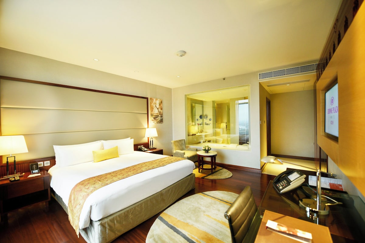 Quarto de hotel com cama grande, área de estar, banheiro com espelho e televisão.