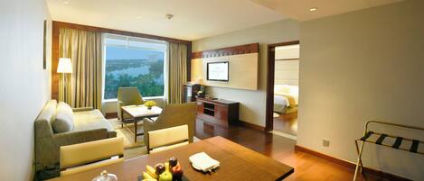 Quarto de hotel com uma mesa de jantar, cadeiras, um sofá, uma televisão e vista para a paisagem urbana.