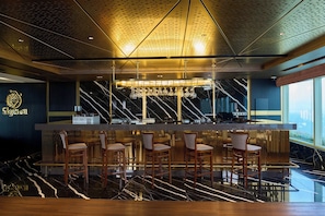 Uma área de bar com piso de mármore, banquetas, balcão e teto com design vazado.