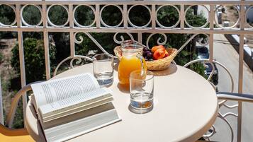Uma mesa com um livro, um copo de sumo de laranja e uma cesta de frutas.